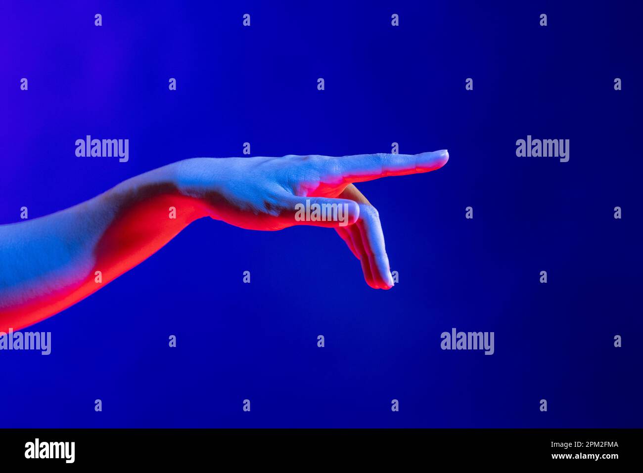Exposed hand pointing finger in studio with blue light with copy space ...