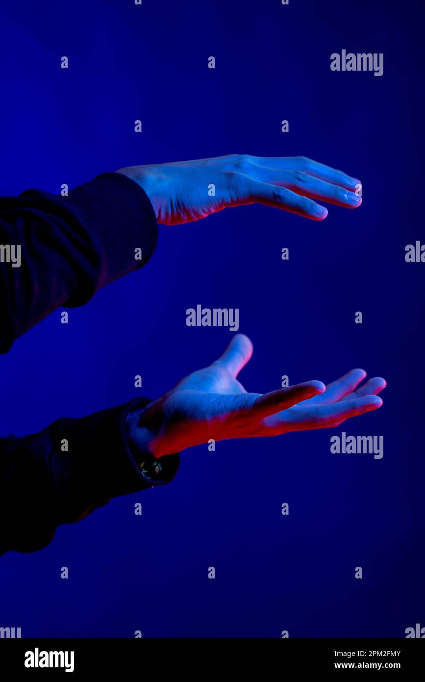 Exposed hands making gestures in studio with blue light with copy space ...