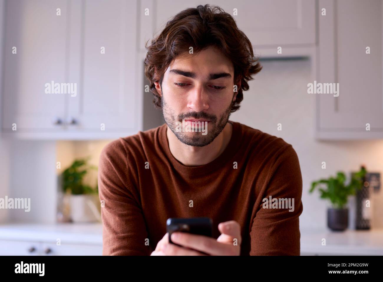 Young Man Relaxing At Home In Kitchen Checking Messages Social Media On ...