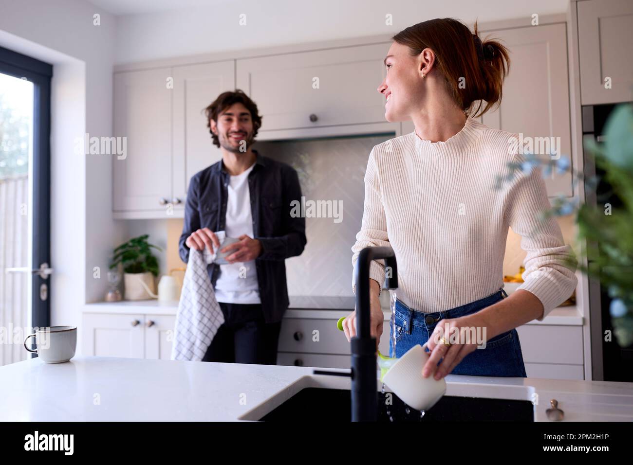 Couple At Home In Kitchen With Woman Doing Washing Up Stock Photo - Alamy