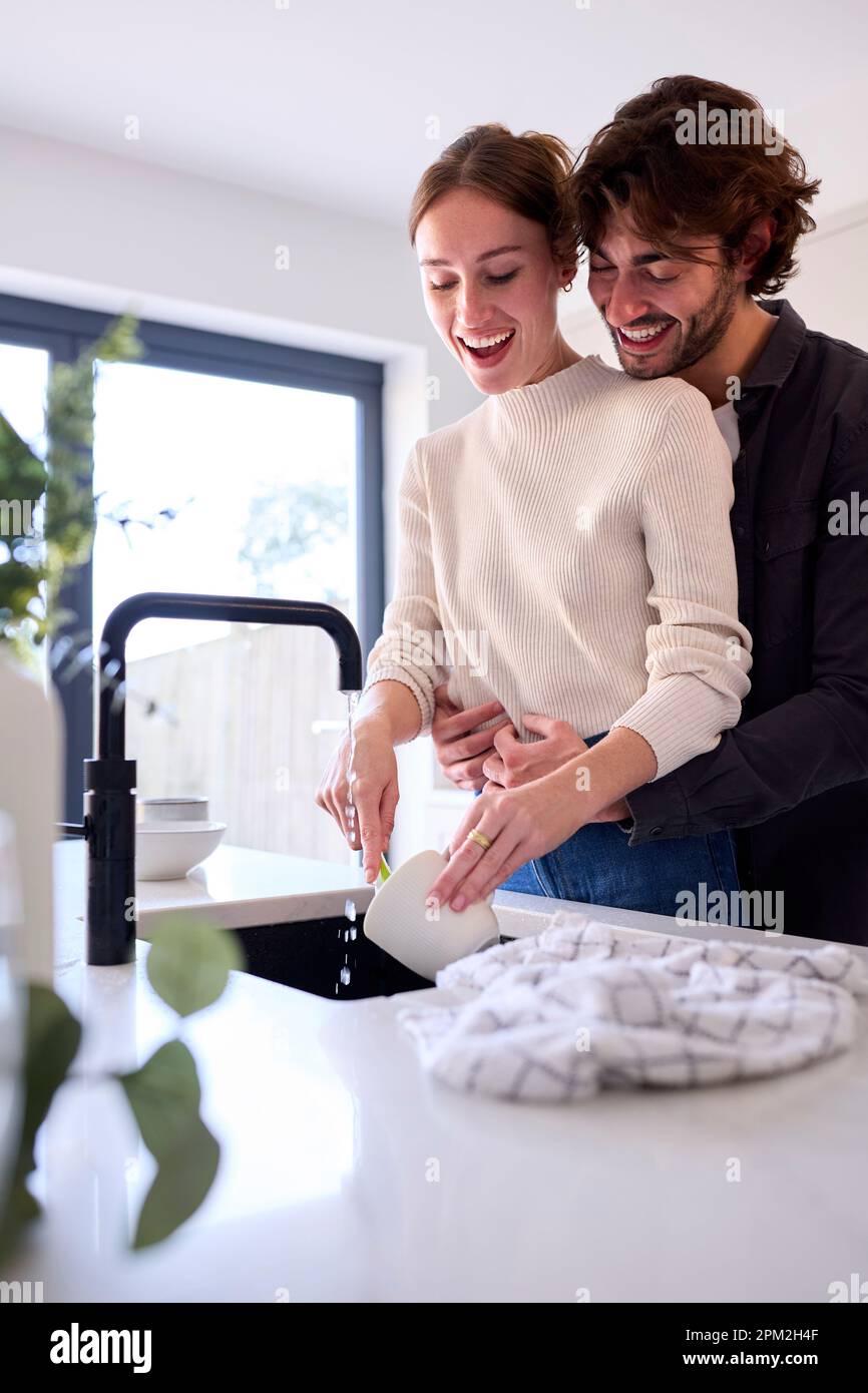 Couple Hugging At Home In Kitchen As Woman Does Washing Up Stock Photo ...