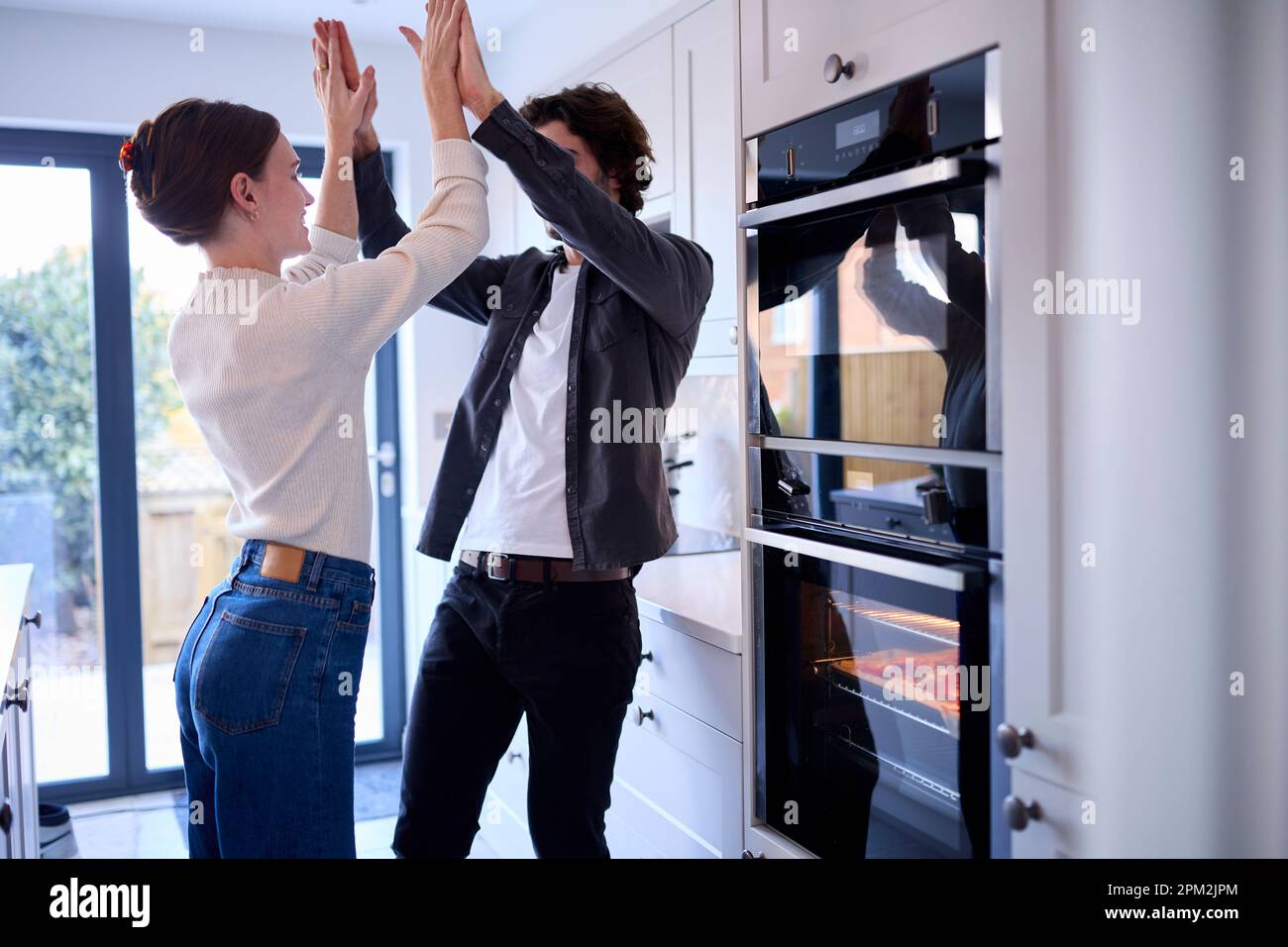 Couple In Kitchen At Home Putting Homemade Pizza Into Oven To Bake ...