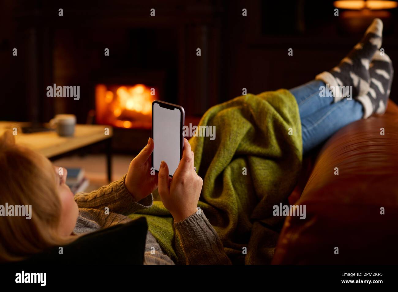 Woman At Home Lying On Sofa In Lounge With Cosy Fire Using Blank Screen ...