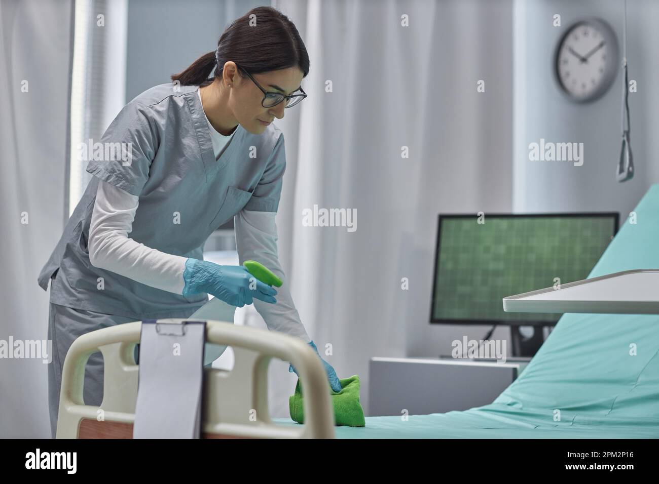 Young nurse using rag and detergent to clean the bed in empty hospital ...