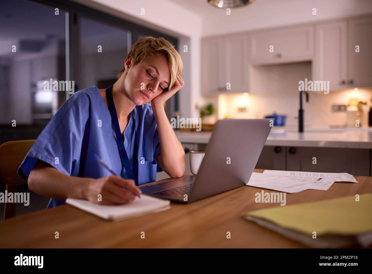 Tired Woman Wearing Medical Scrubs Working Or Studying On Laptop At ...