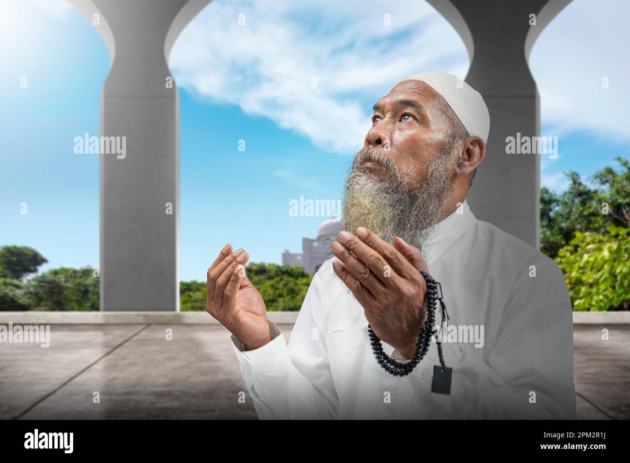 Muslim man with a beard wearing a white cap praying with prayer beads ...