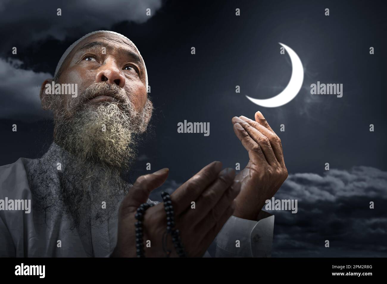 Muslim man with a beard wearing a white cap praying with prayer beads ...