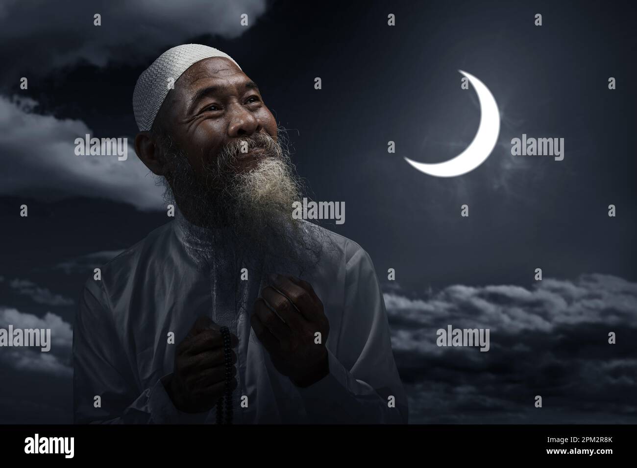 Muslim man with a beard wearing a white cap praying with prayer beads ...