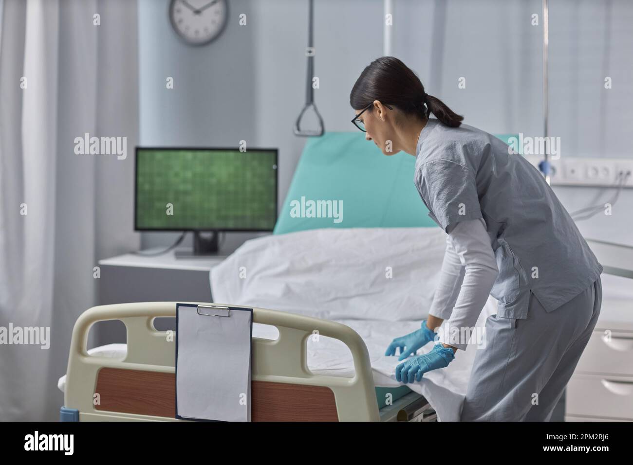 Nurse in uniform making bed with clean bedsheet preparing it for ...