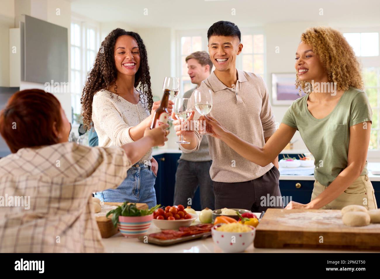 Group Of Friends At Home In Kitchen With Drinks Making Food For Party ...