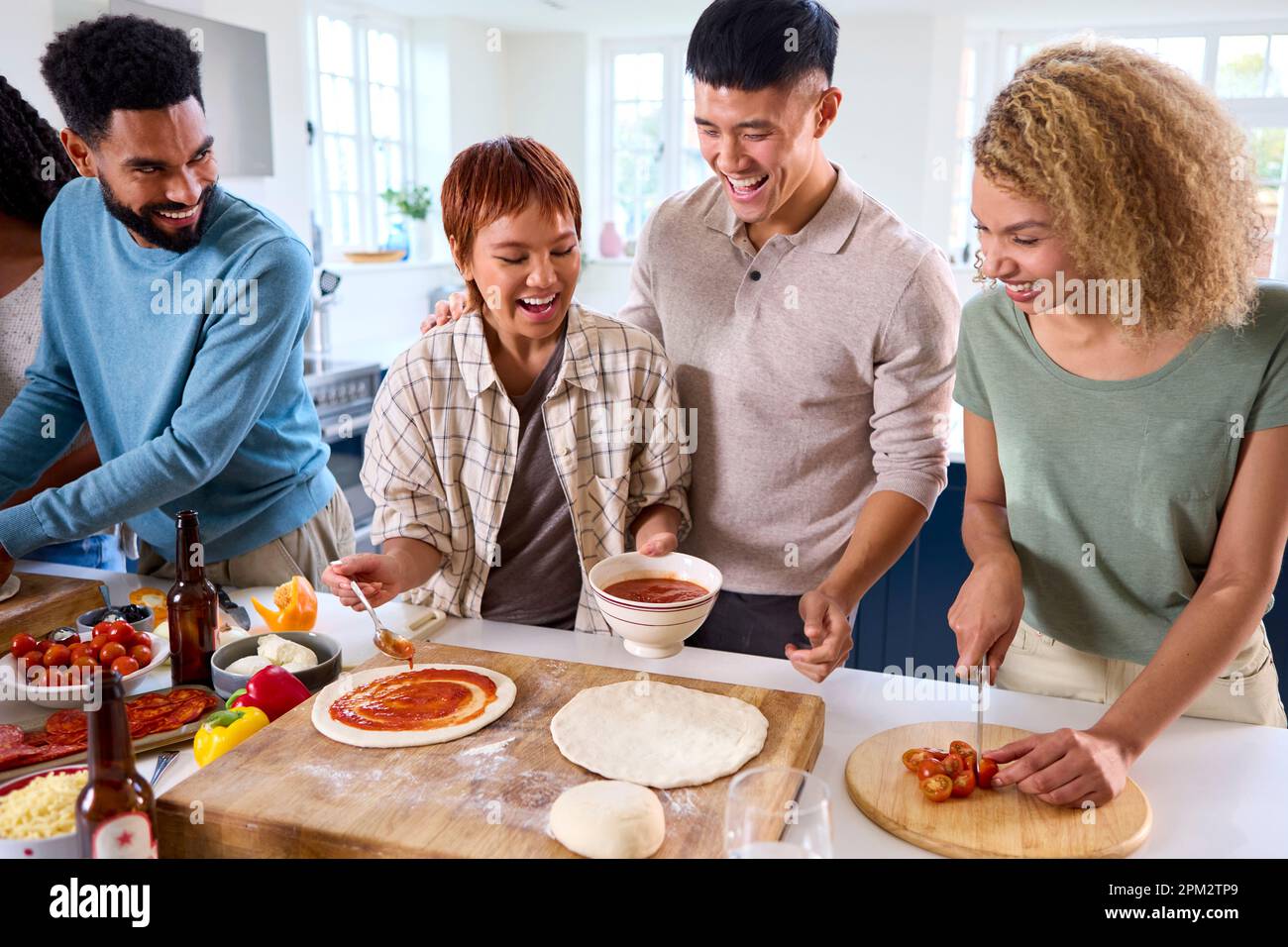 Group Of Friends At Home In Kitchen Adding Sauce To Homemade Pizzas For ...