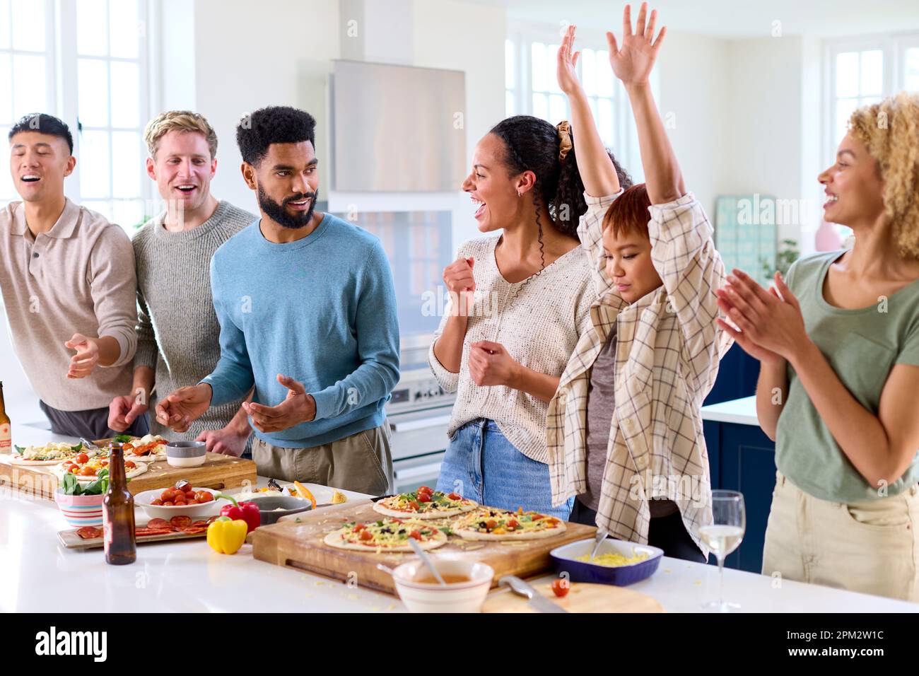 Group Of Friends At Home In Kitchen Adding Toppings To Homemade Pizzas ...