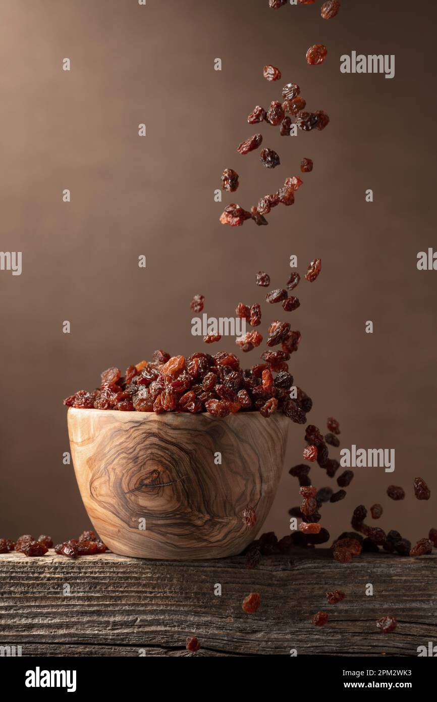 Flying raisins on a brown background. Raisins in a wooden bowl. Copy ...