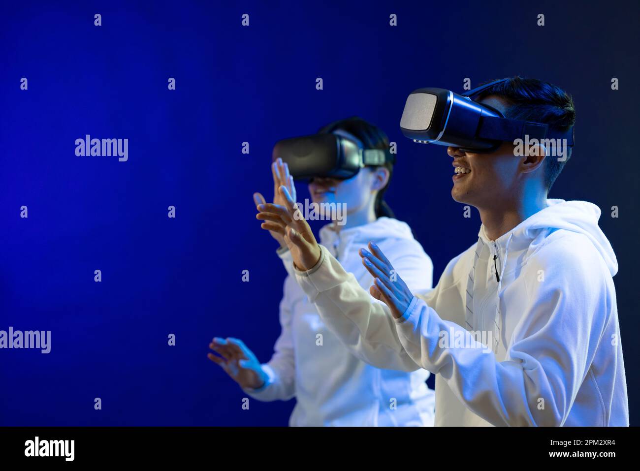 Happy asian man and woman using vr headsets in studio with blue light ...
