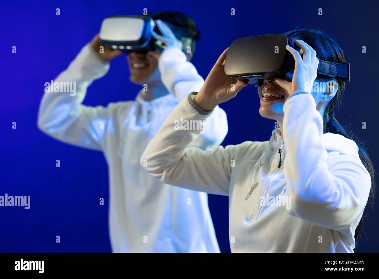 Happy asian man and woman holding vr headsets in studio with blue light ...