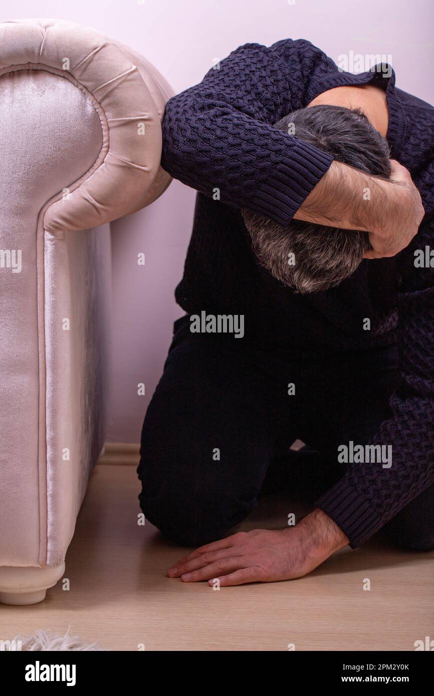 Man protected from earthquake. Frightened man hiding next to sofa in ...