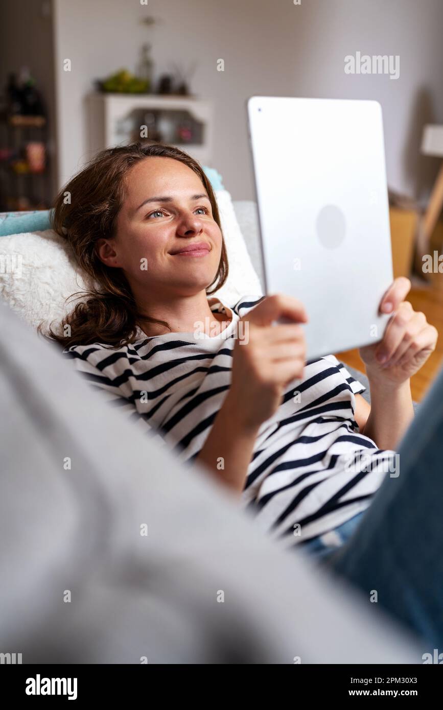 A brunette woman lies on a sofa and watches social media videos on the ...