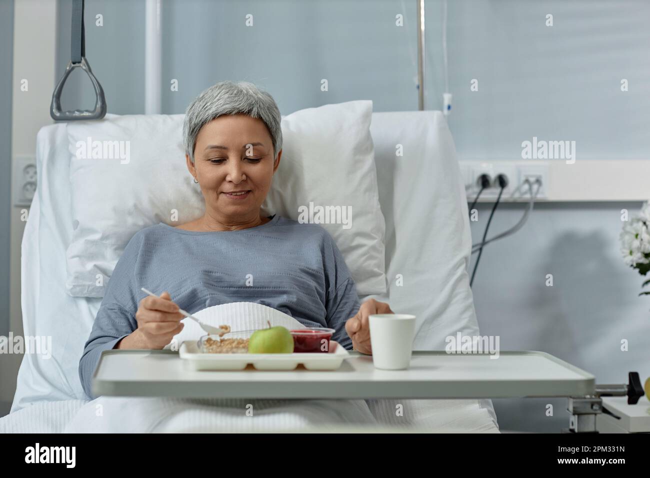 Mature woman sitting on bed and eating healthy food during lunch in ...