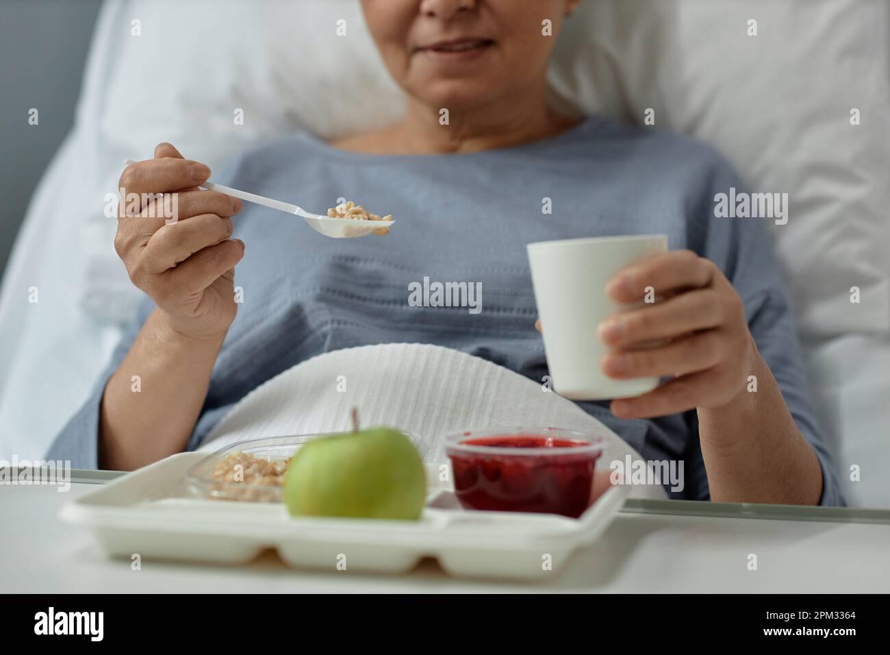 Close-up of senior patient sitting on bed with tray and eating healthy ...