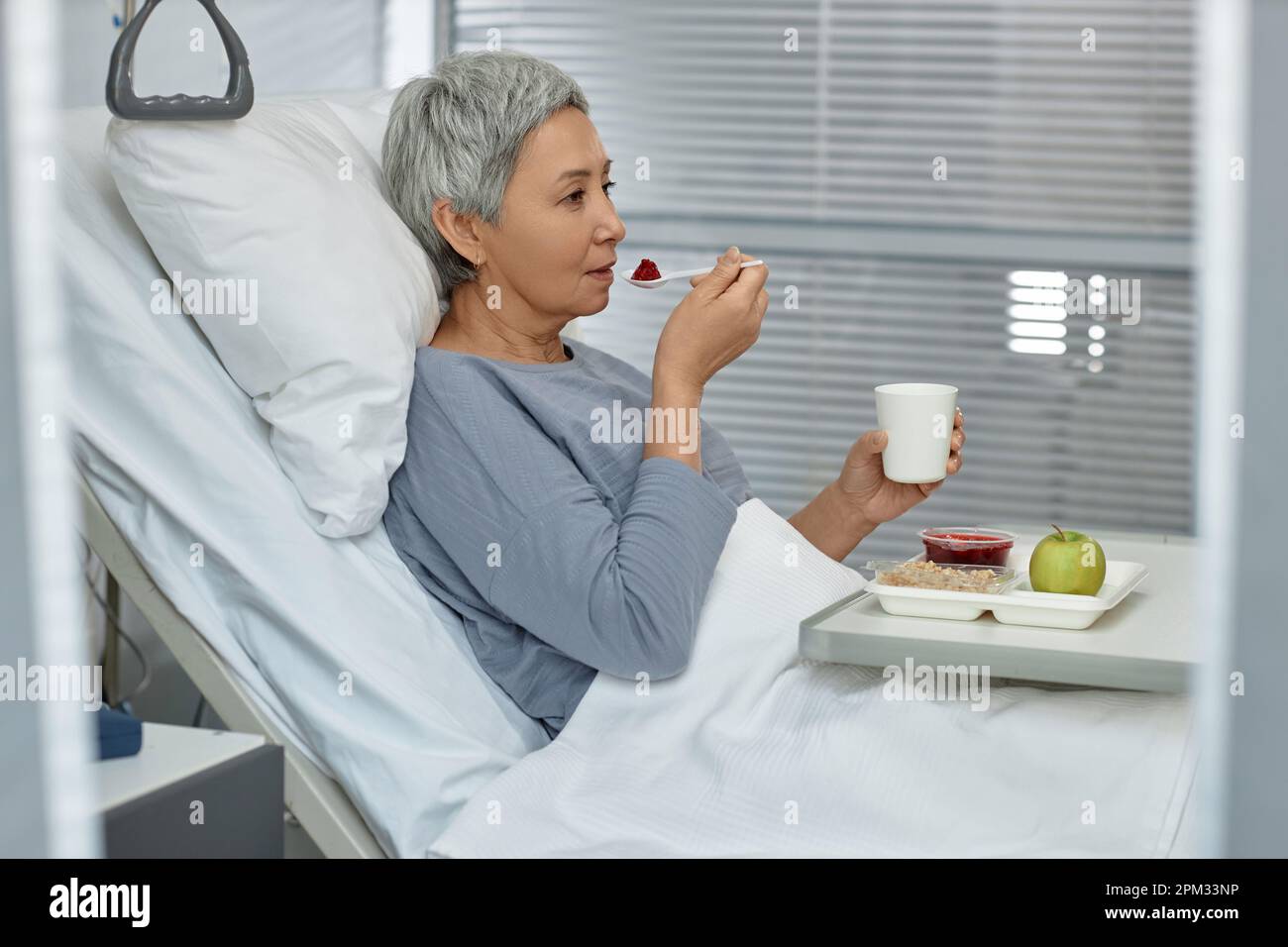 Senior sick woman eating healthy food while sitting on her bed in ...