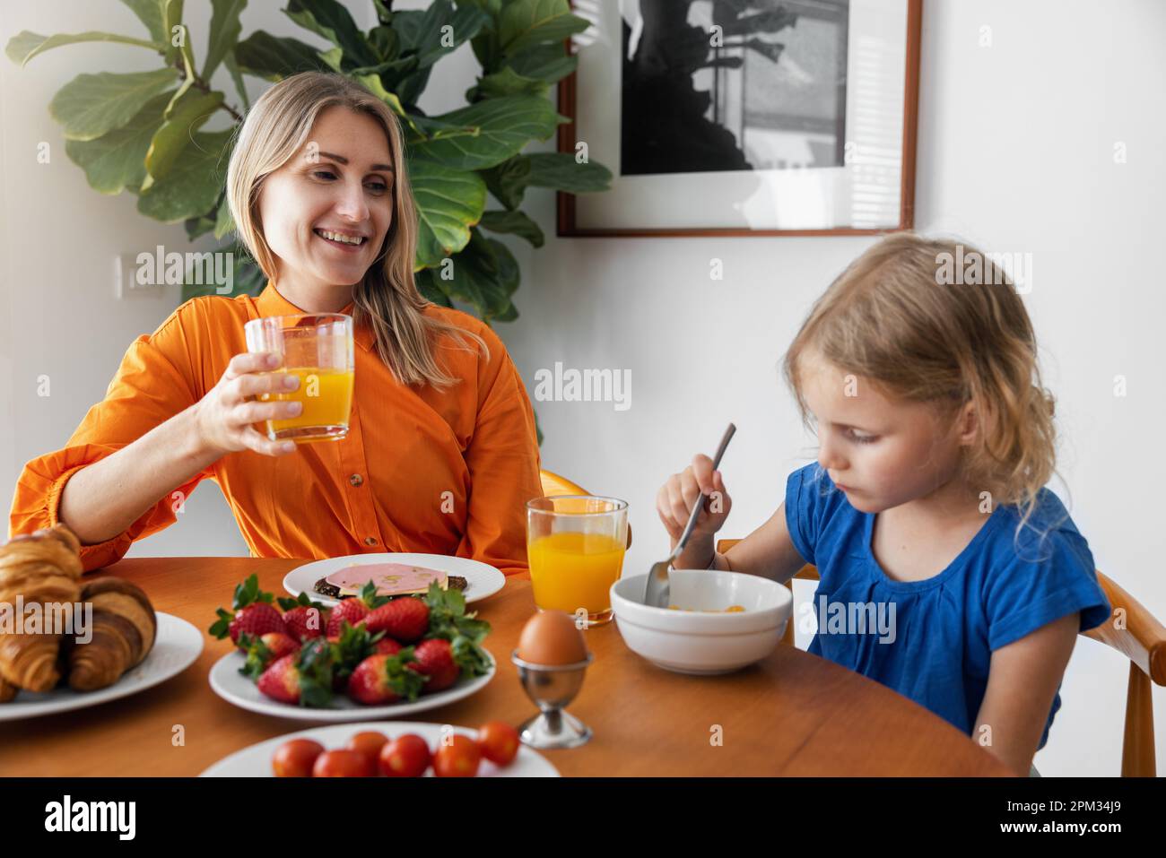 mother and daughter eating breakfast at home. sitting by the table in ...