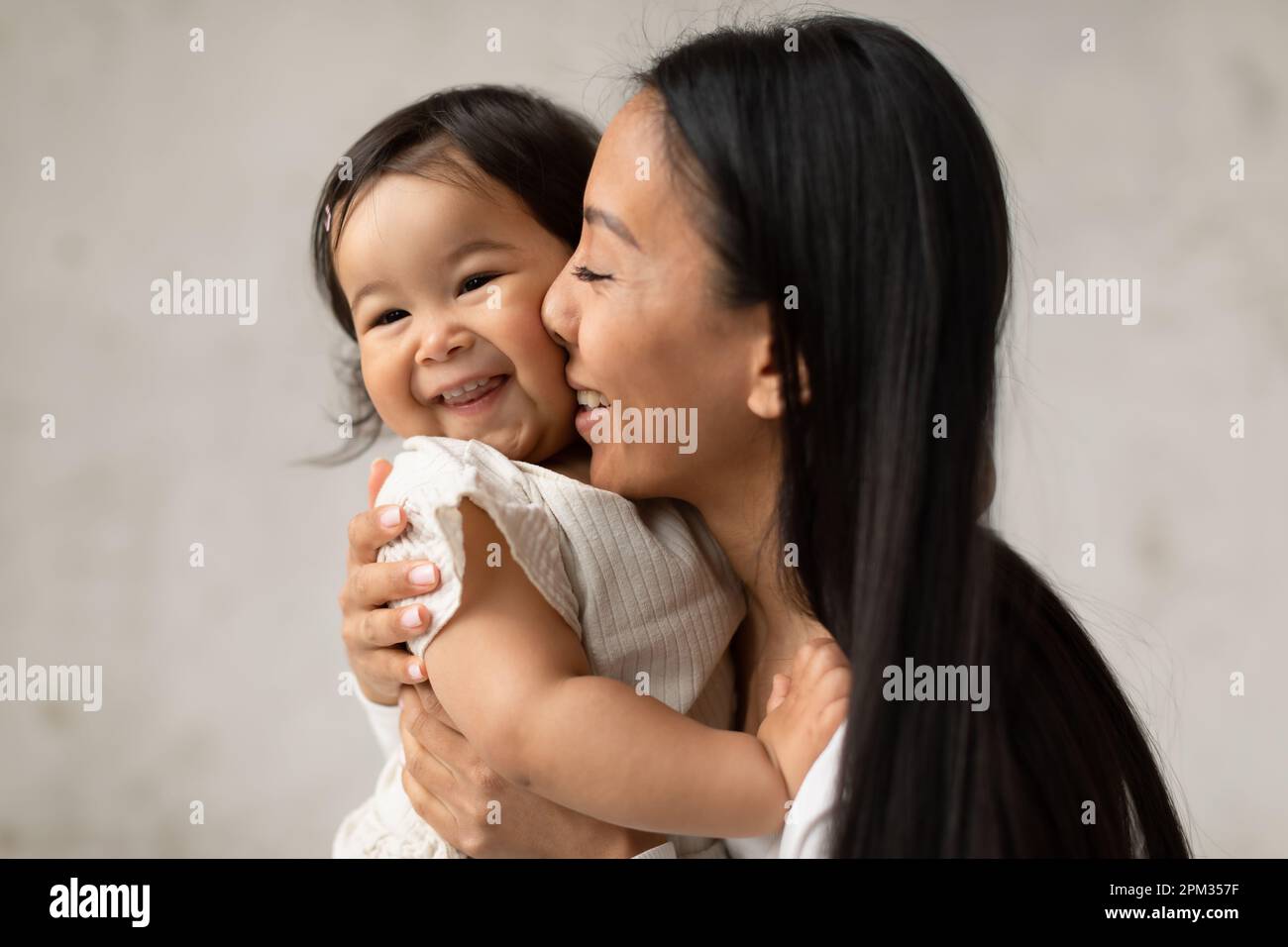 Happy Japanese Mother Rubbing Nose On Baby Daughter's Cheek Indoors ...