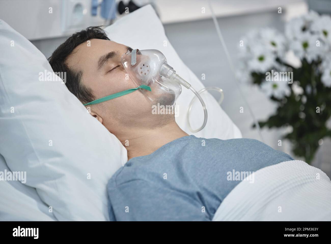 Young patient with oxygen mask lying in hospital ward during his ...
