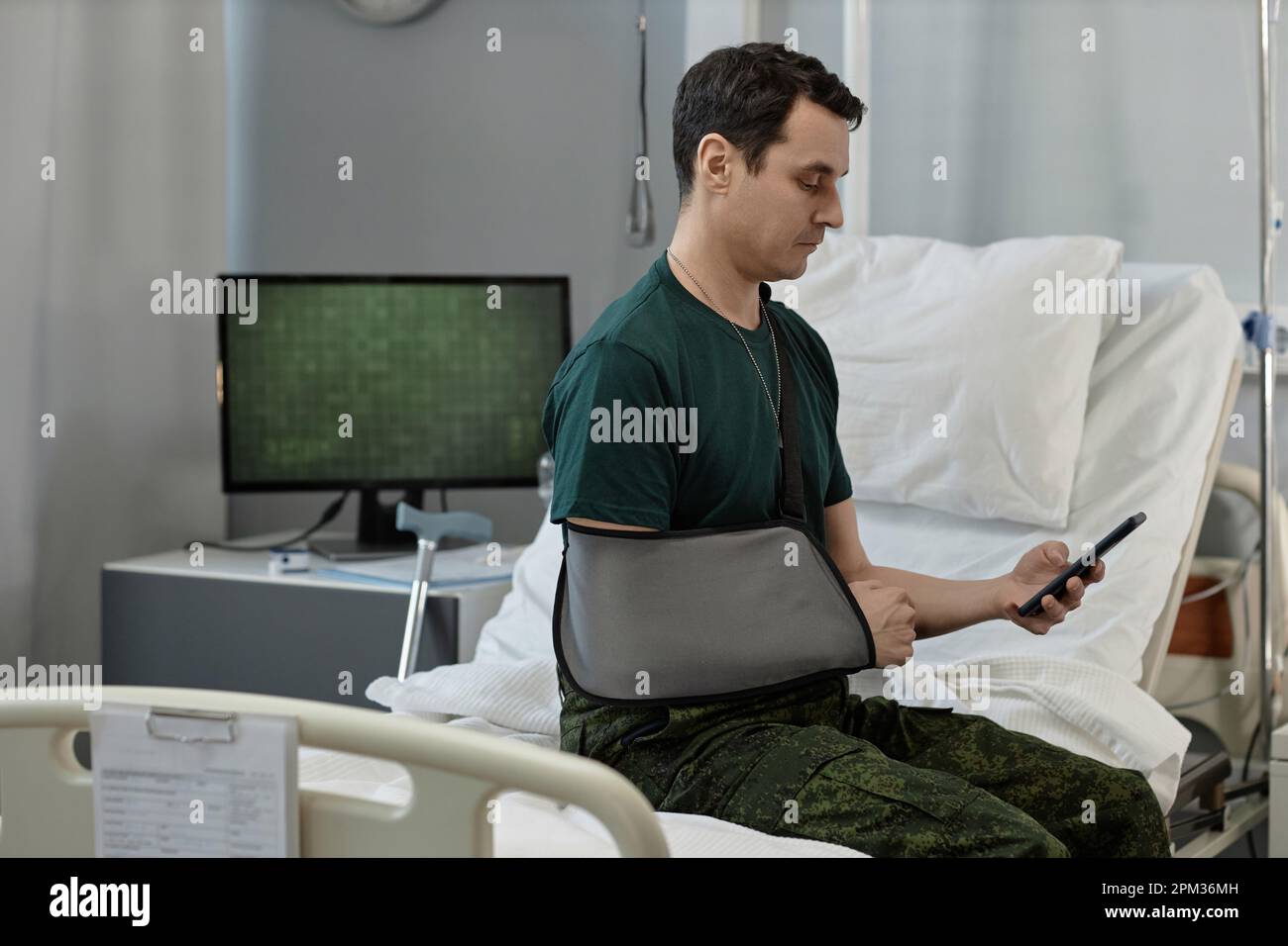 Soldier with injured arm in bandage reading message on smartphone while ...