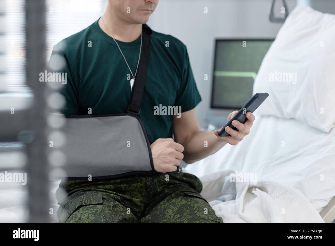 Young soldier in bandage on his arm reading message on his mobile phone ...