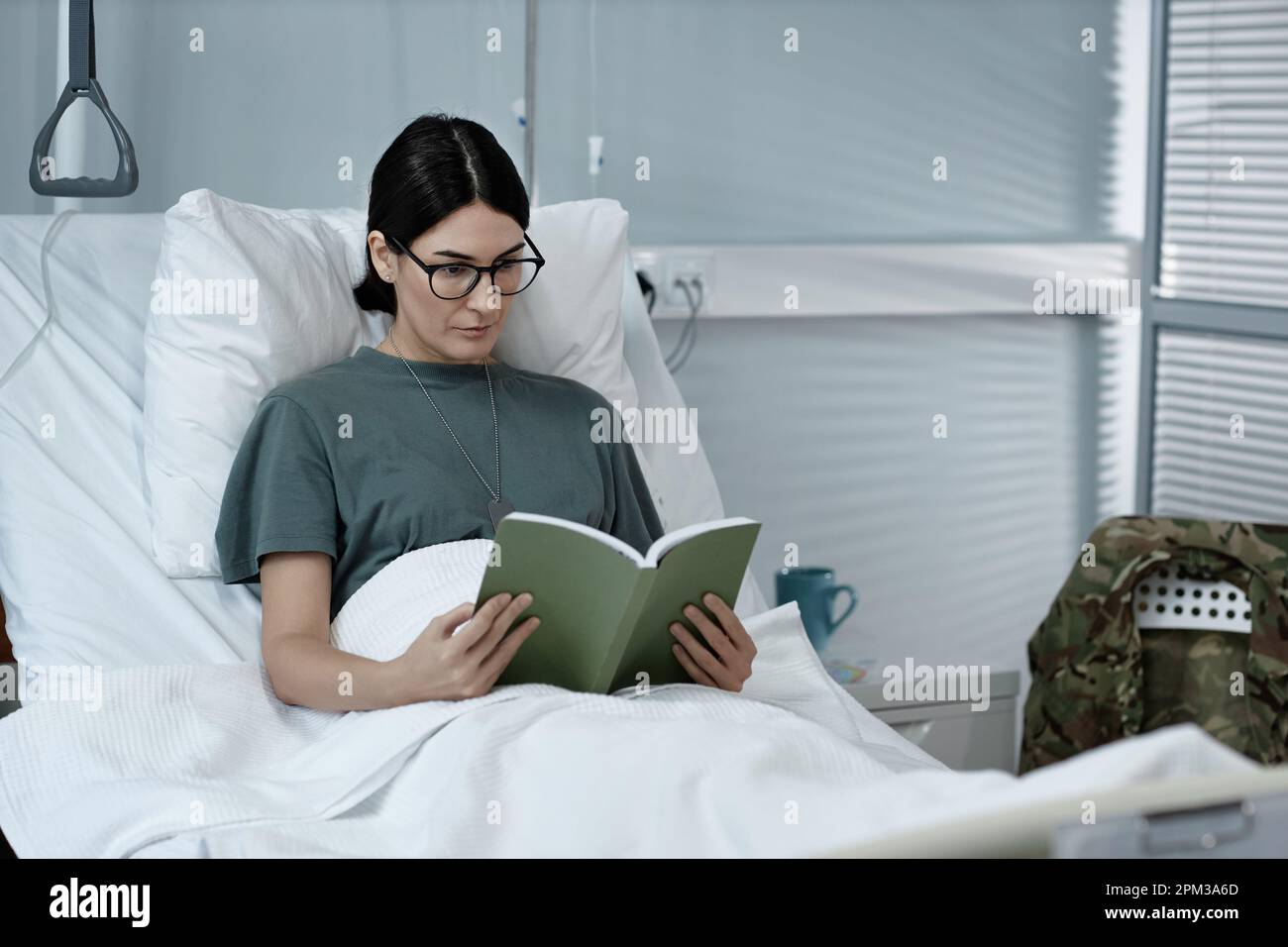 Female soldier reading a book while lying on bed in hospital ward ...