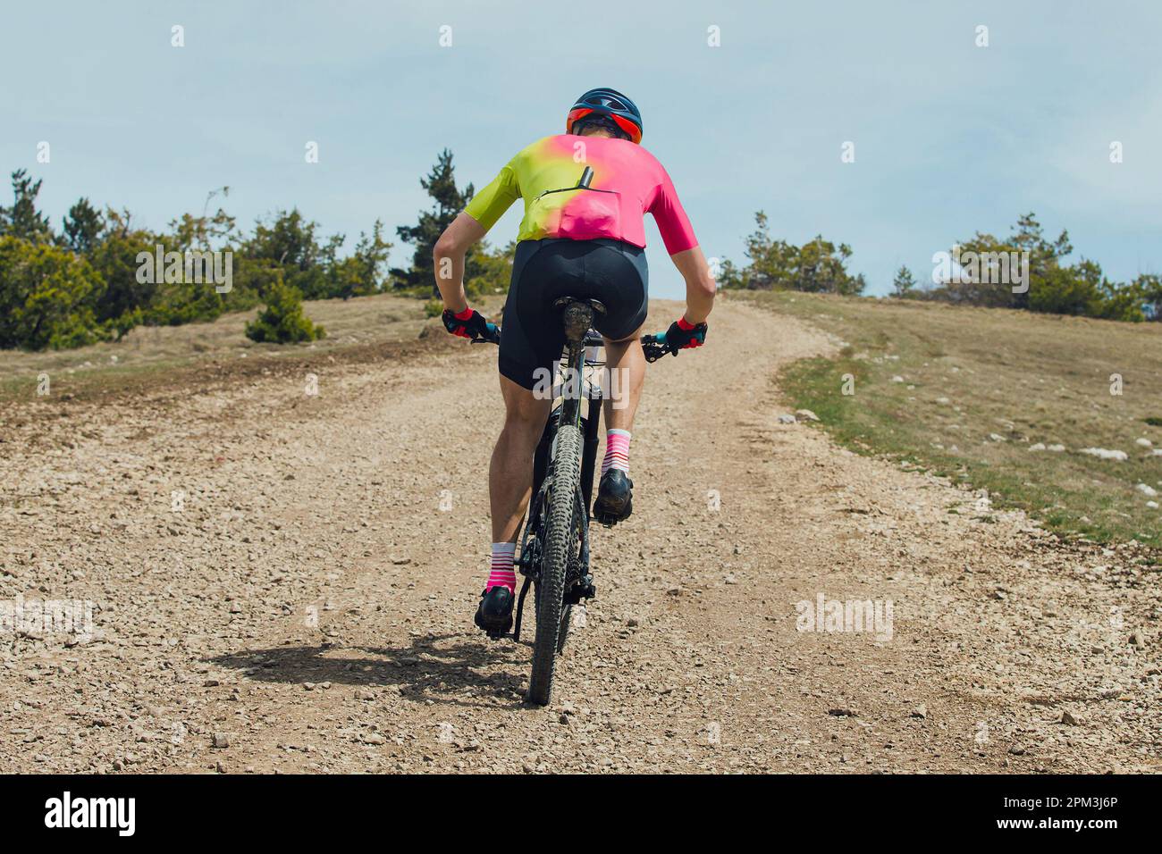 rear view athlete cyclist riding mountain bike uphill, biking on gravel ...