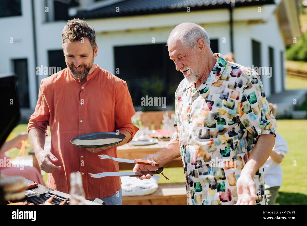 Senior father with adult son grilling outside on backyard in summer ...