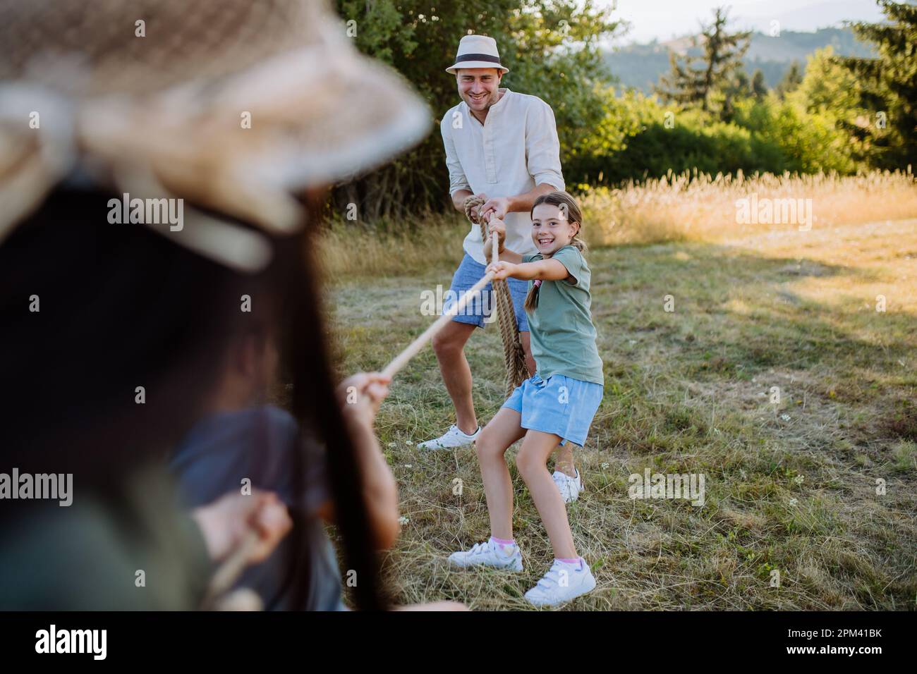 Young family with happy kids having fun together outdoors pulling rope ...