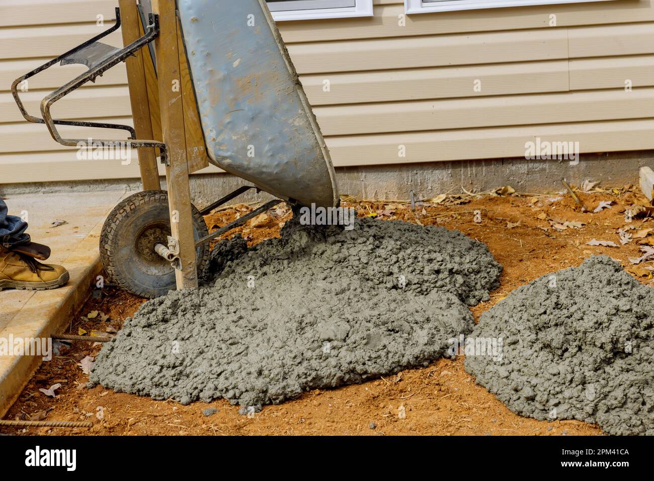 Construction worker pours cement from wheelbarrow to create concrete ...