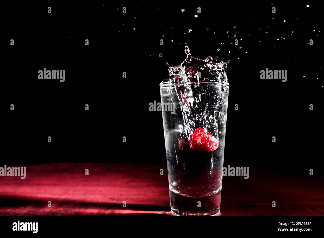 A close-up image of a single raspberry falling into a glass of water ...