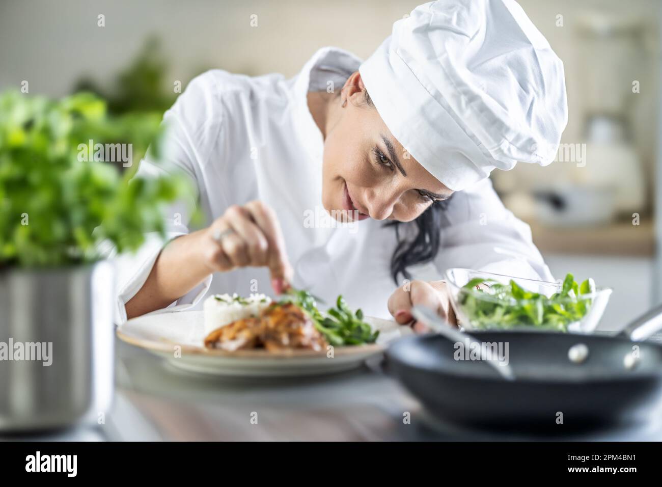 A young female chef finishes the meal with herbs in the restaurant ...