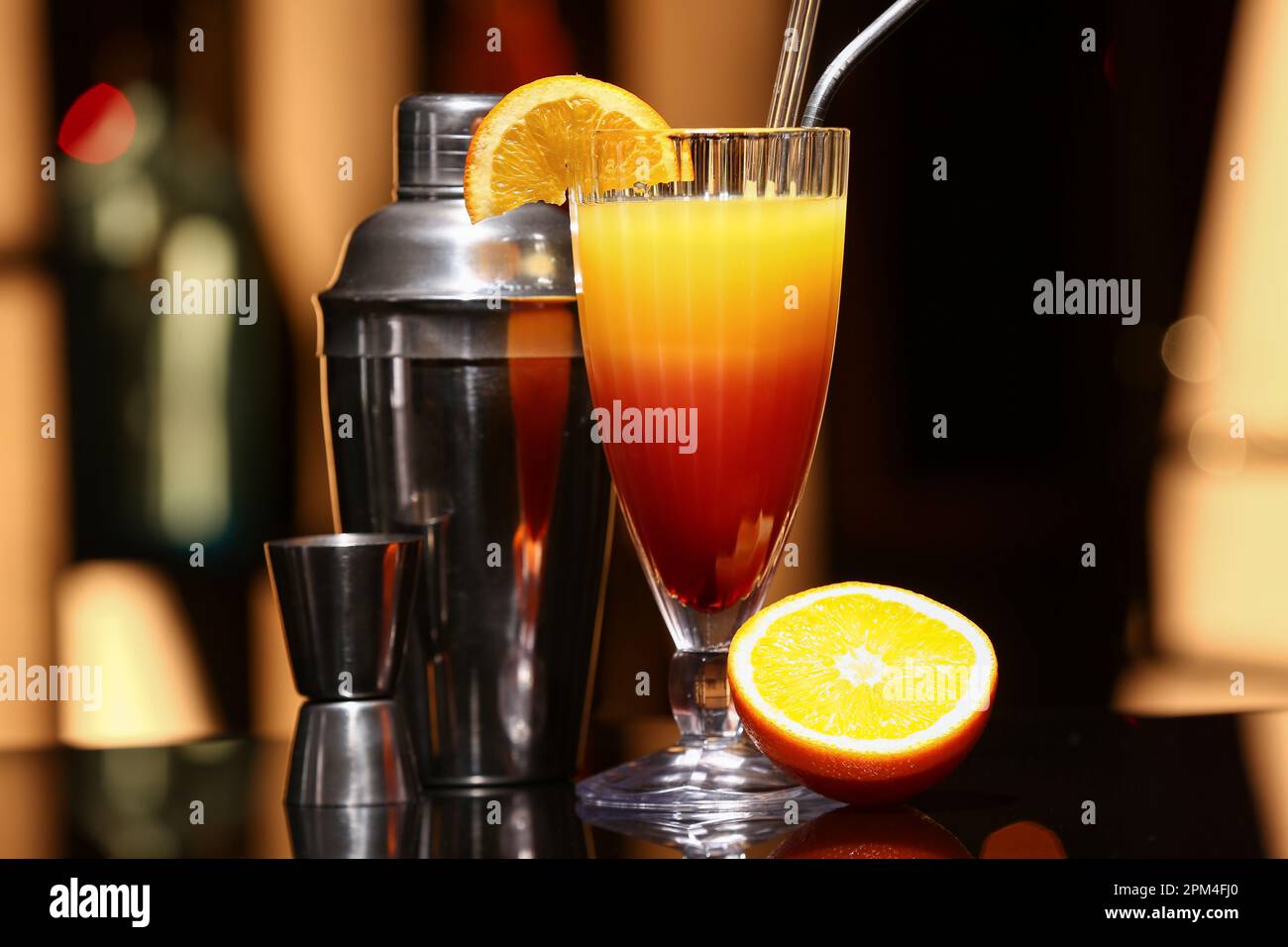 Glass of tasty Tequila Sunrise, cocktail shaker and double jigger on ...
