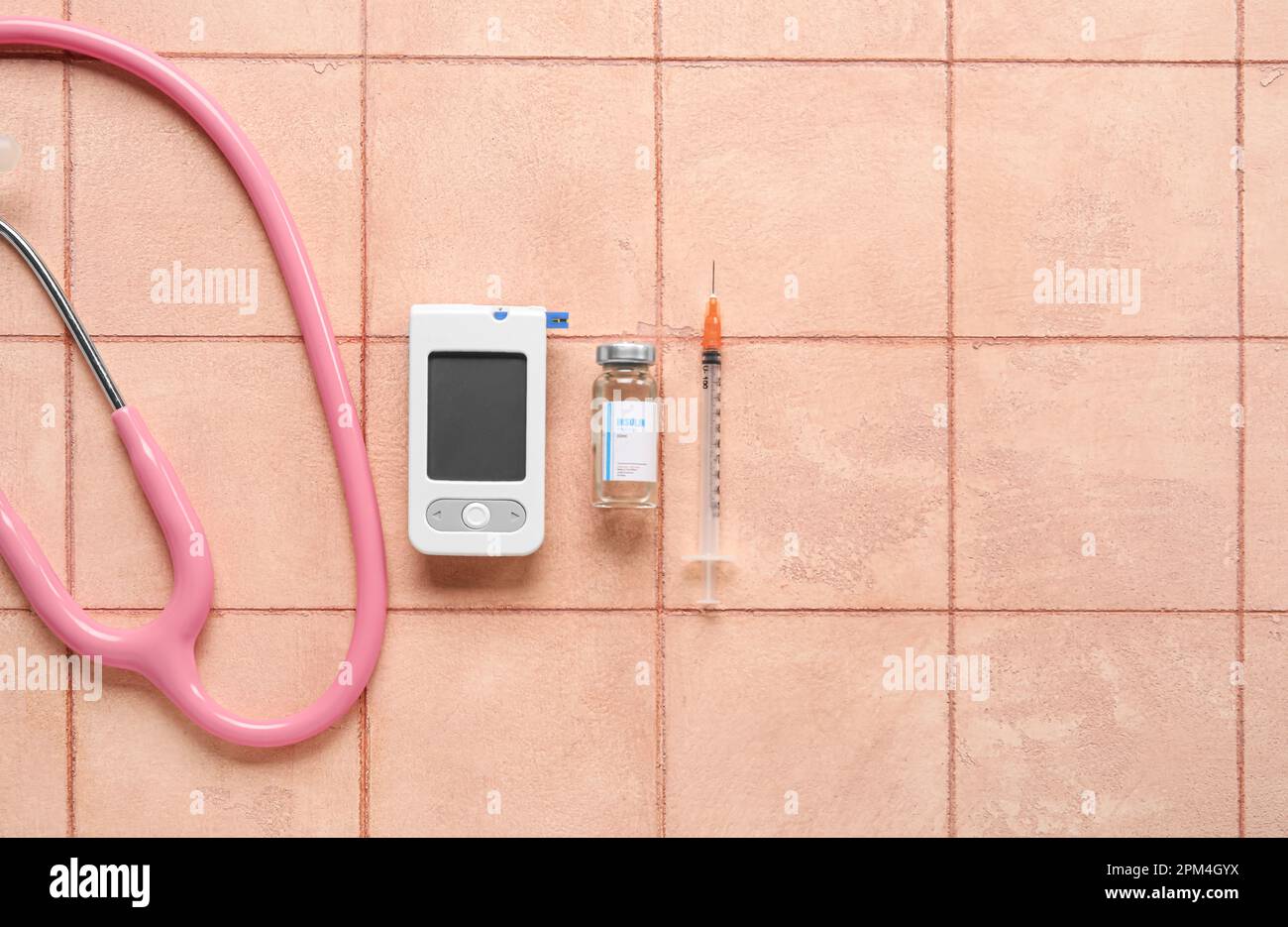 Glucometer with insulin, syringe and stethoscope on pink tile ...