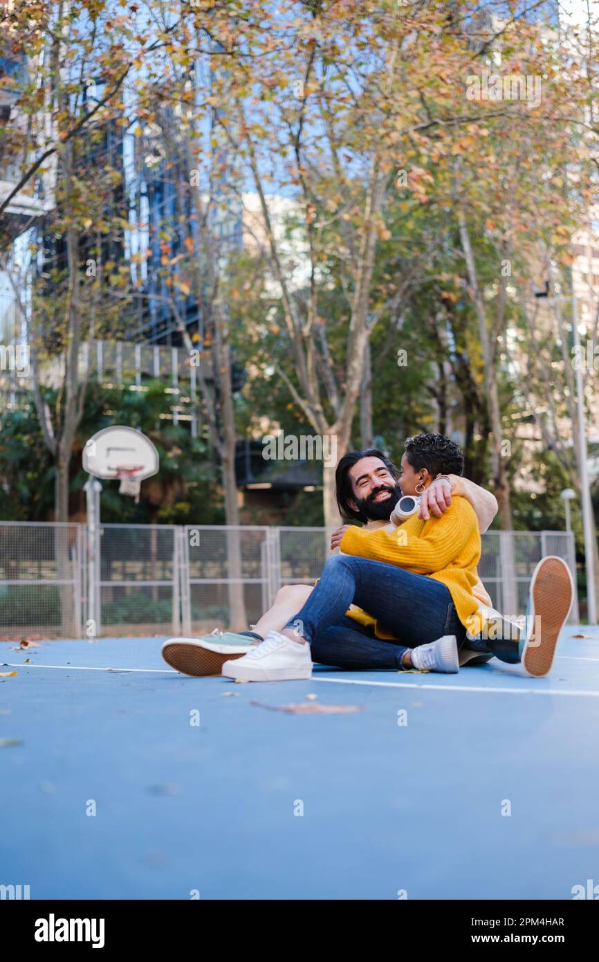 Couple lying on the floor of the basketball court embracing and smiling ...