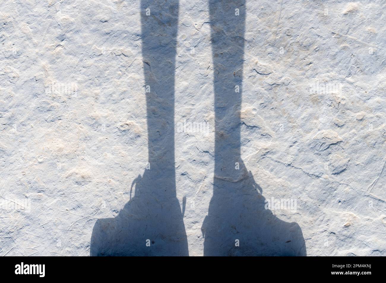 The shadow of a man's legs against the white rock ground of the white ...