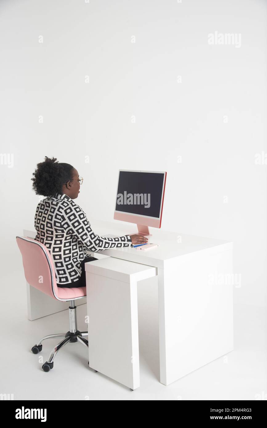 England, UK. 2023. Secretarial worker seated in a pink chair using a ...