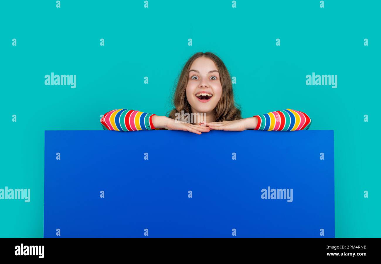 happy shocked child behind blank blue paper with copy space for ...