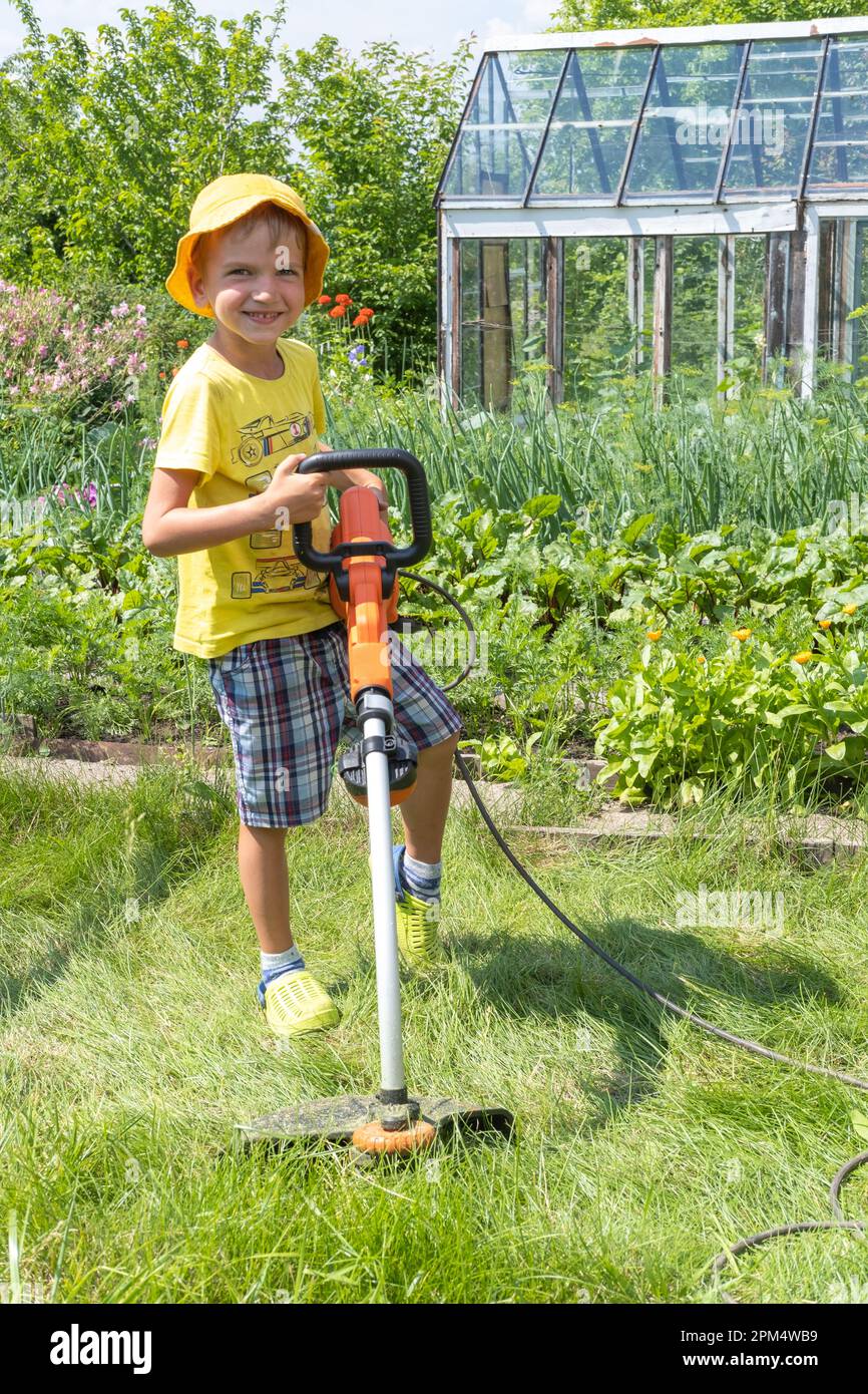 Portrait a boy with an electric lawn mower mowing the lawn. Beauty boy ...