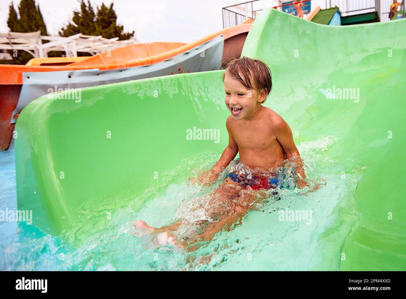 Cheerful blue-eyed kid on a water slide in the water park, a little boy ...
