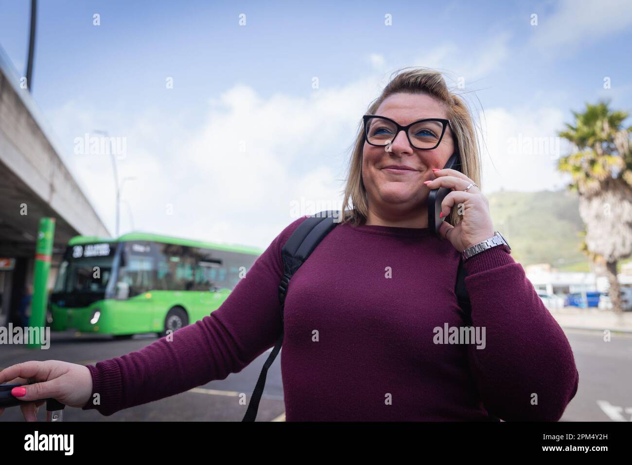 A smiling young woman makes a phone call while waiting for the bus at ...
