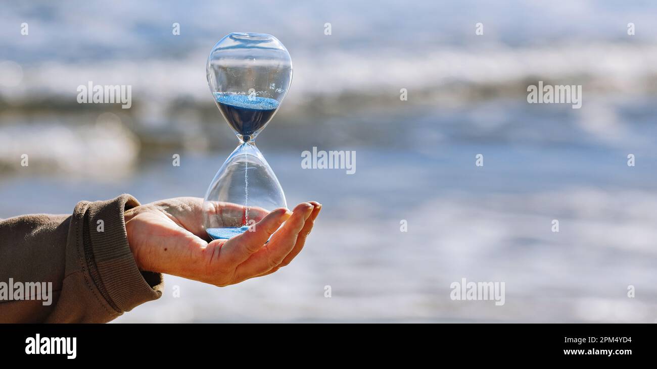 Time is running fast. Hourglass with blue sand inside in mature woman's ...