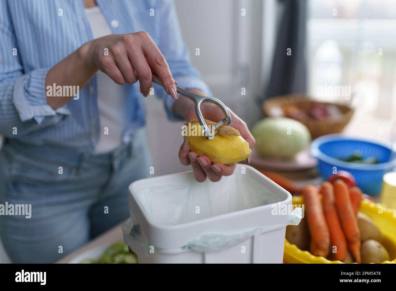 Female person peeling potato and recycling peels in a compost bin ...