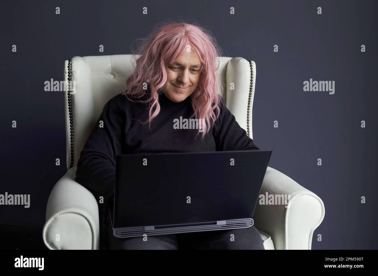 A man in a pink wig sits in a white chair and works at a computer Stock ...