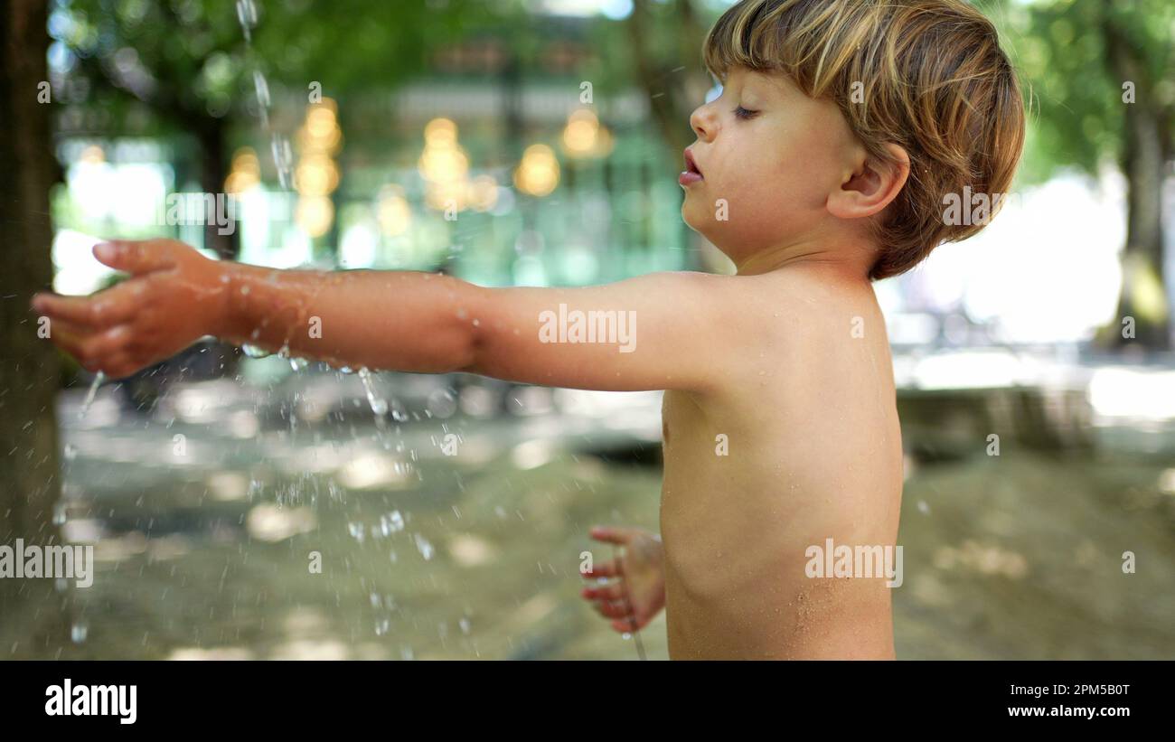 Child washing hands and body at public water park fountain outside in ...