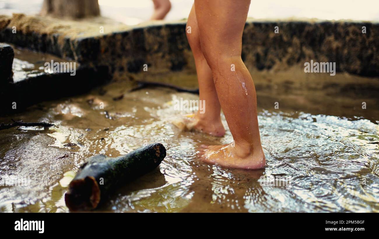 Child legs and feet walking in puddle water with mud barefoot during ...